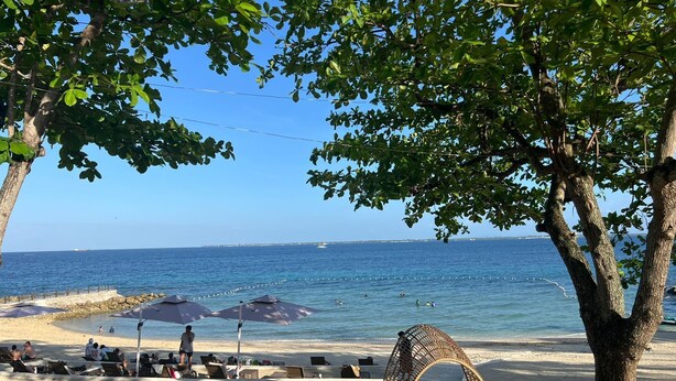 Uma praia com guarda-sóis, cadeiras de praia e uma área de estar com sombra.