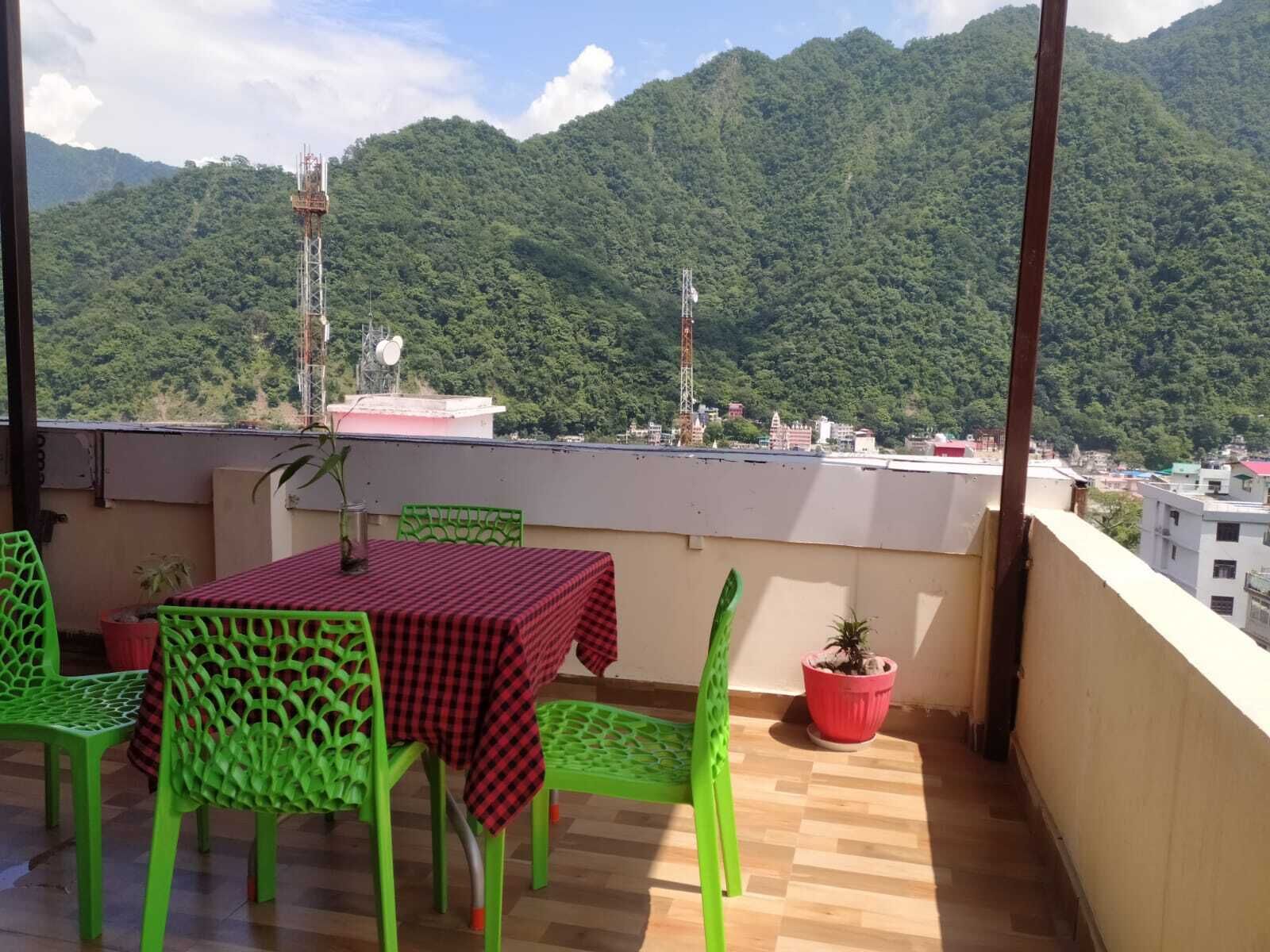 Uma varanda com mesa e cadeiras, um vaso com planta e vista para uma paisagem montanhosa.