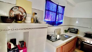 Uma cozinha com bancada branca, janela com cortina azul e pia.