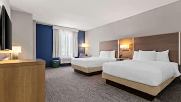 Quarto de hotel com duas camas, uma escrivaninha, televisão e janela com cortinas.