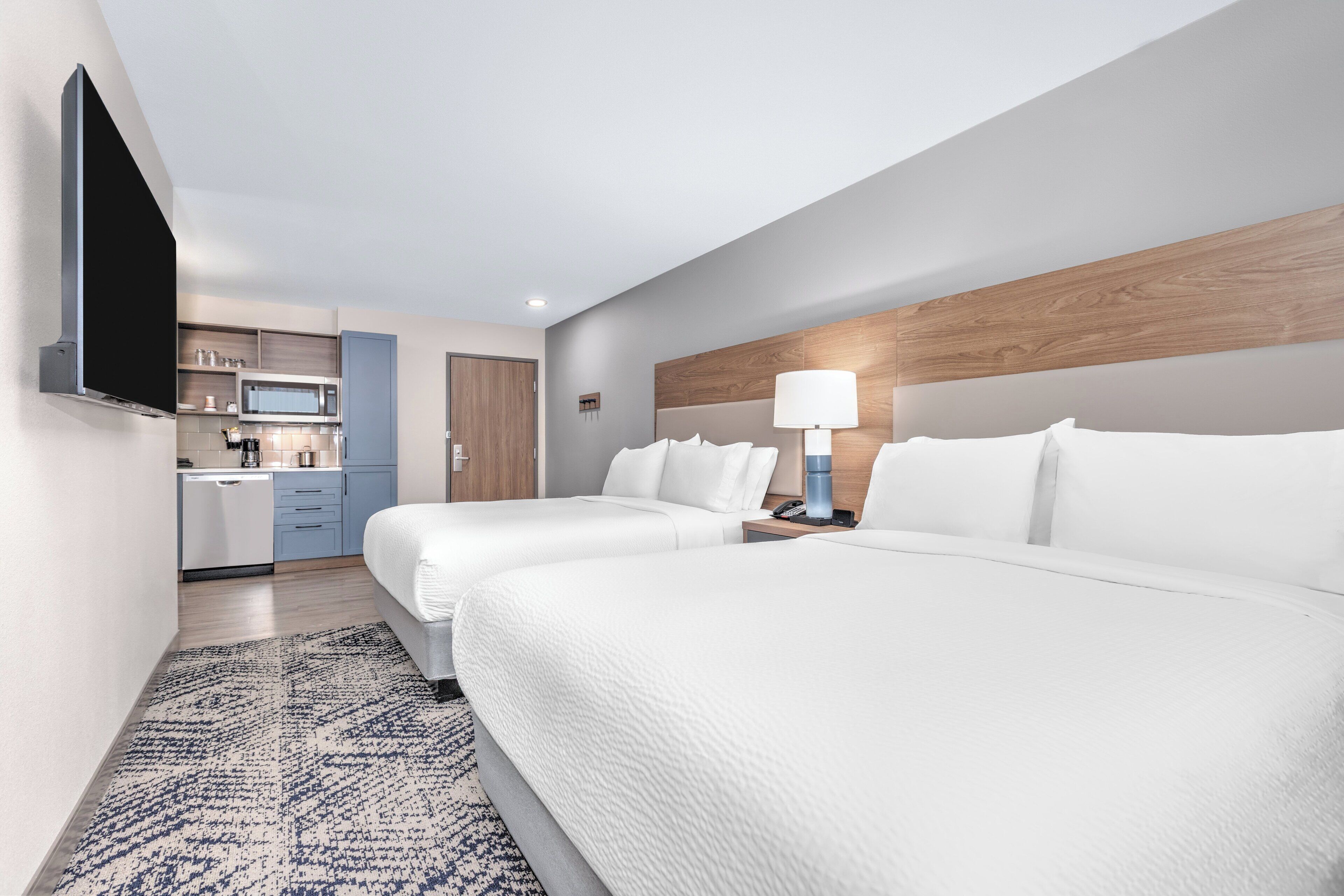 Quarto de hotel com duas camas, televisão, secretária com candeeiro e kitchenette.