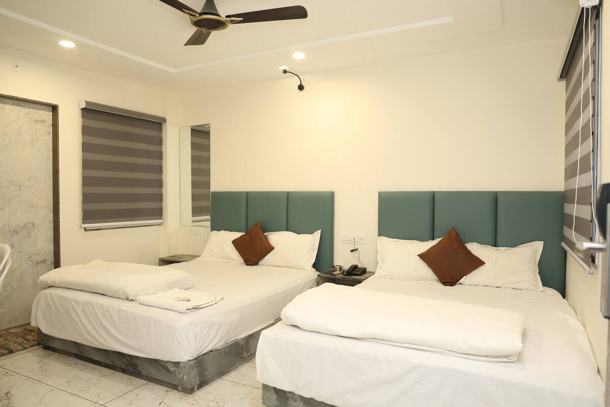 Quarto de hotel com duas camas, um ventilador de teto, mesa de cabeceira com telefone e janela com persianas.