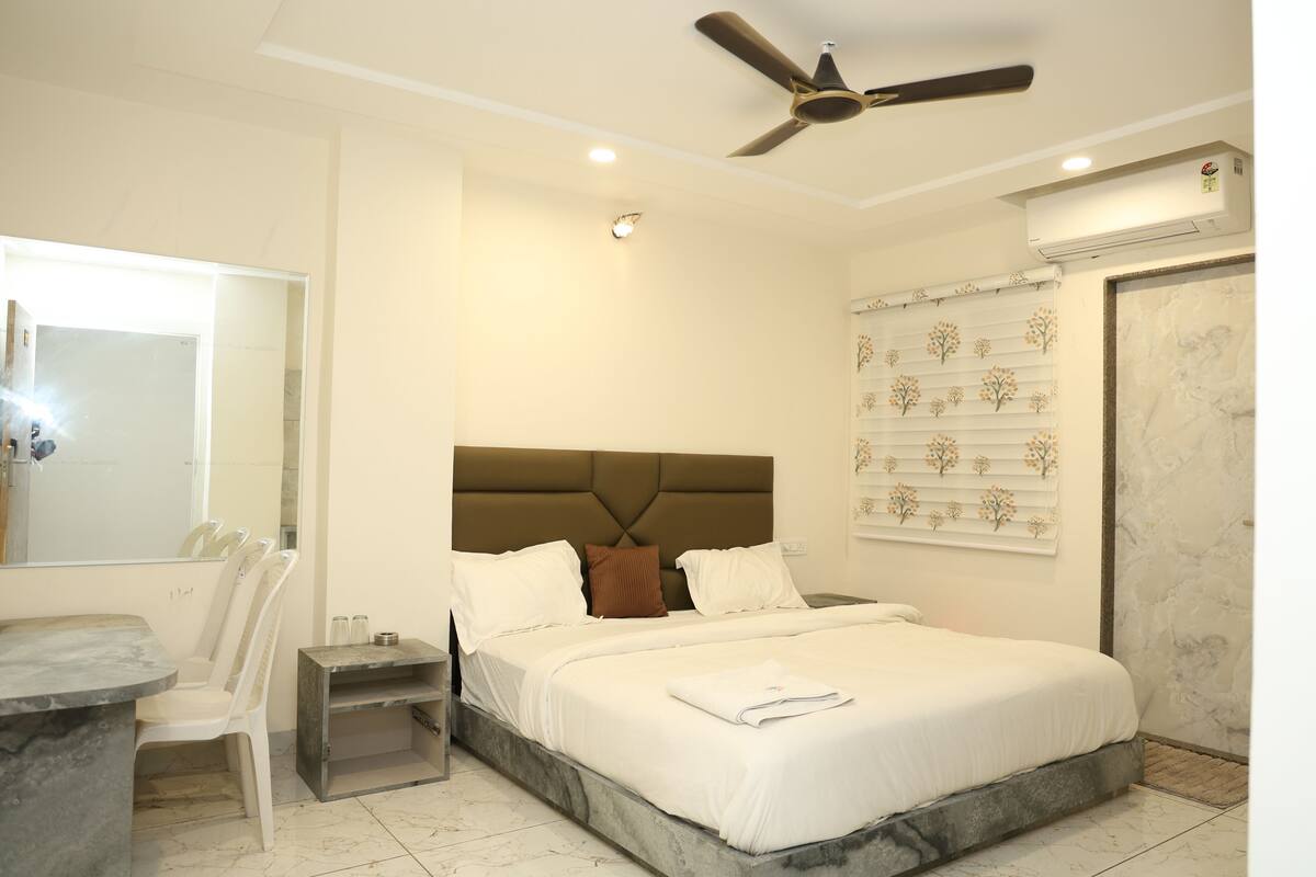 Quarto com cama, mesa de cabeceira, cadeira, ventoinha de teto e ar condicionado fixado na parede.