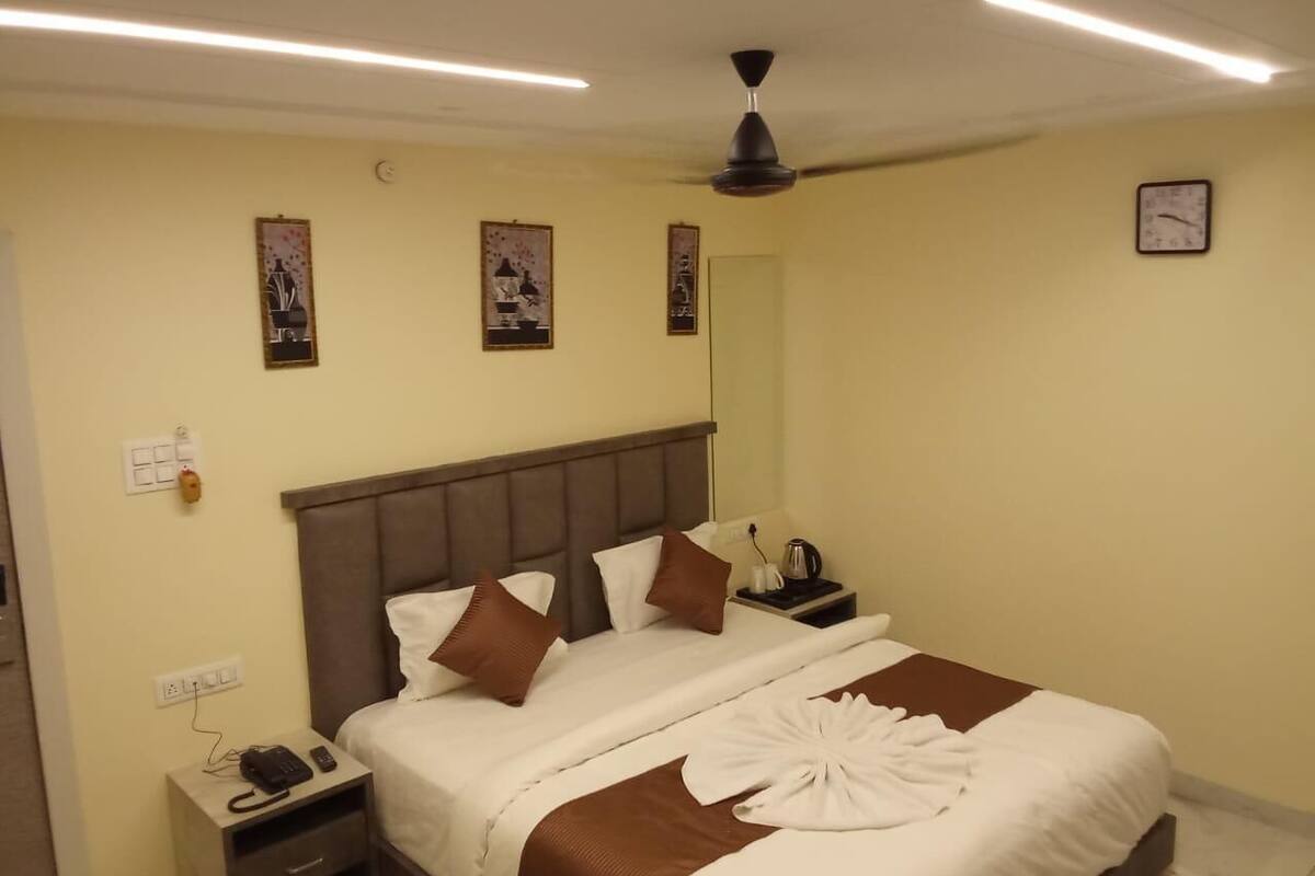 Quarto de hotel com cama, mesa de cabeceira e relógio de parede.