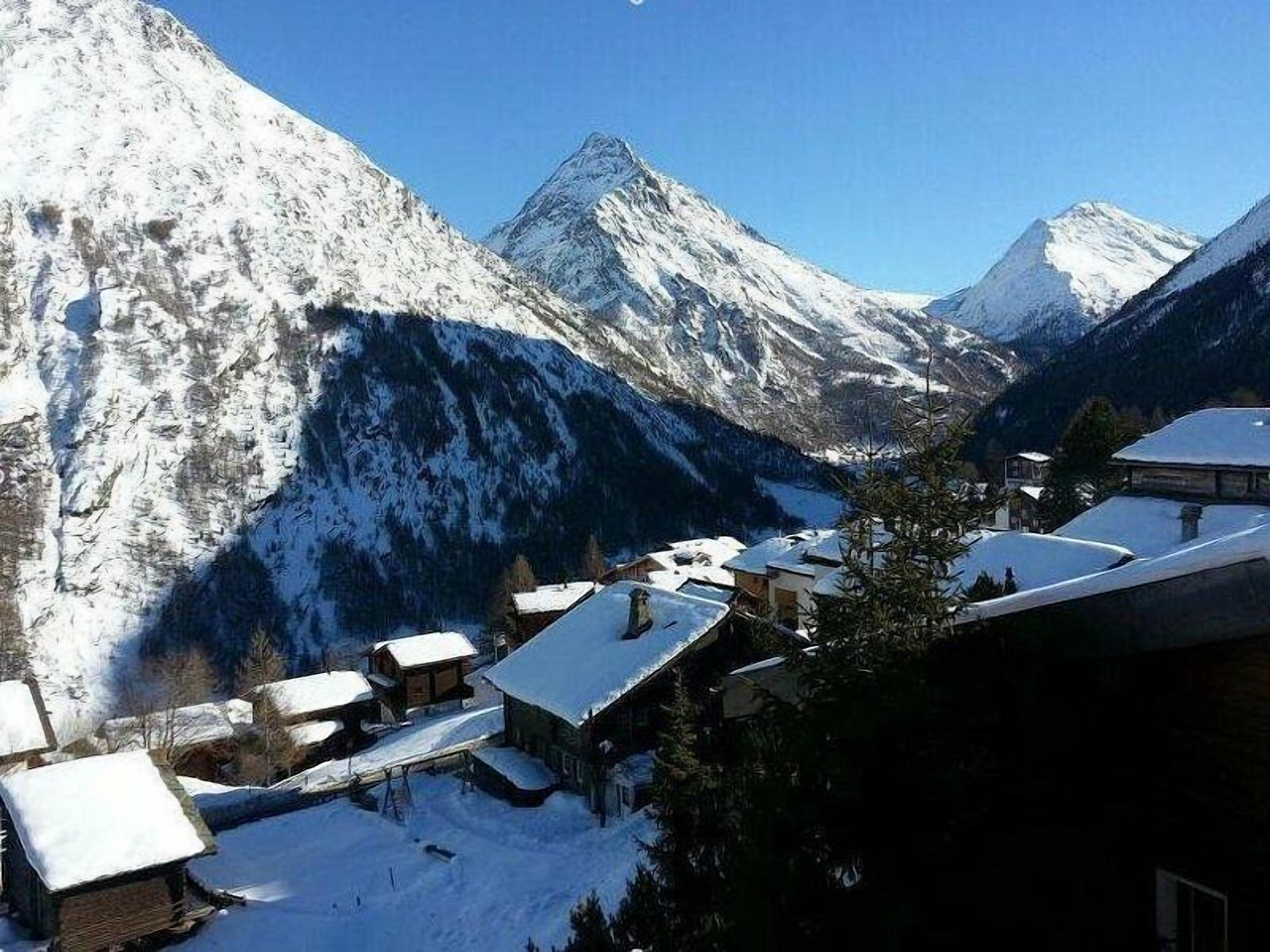 Uma aldeia montanhosa coberta de neve, com casas de madeira tradicionais e uma vista desobstruída dos picos circundantes.