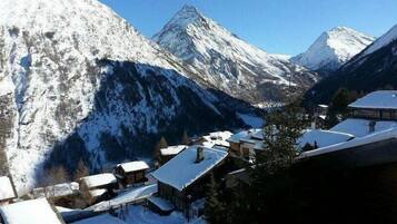 Uma aldeia montanhosa coberta de neve, com casas de madeira tradicionais e uma vista desobstruída dos picos circundantes.