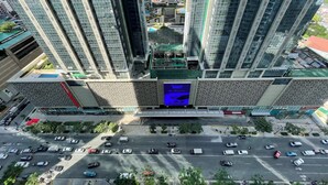 Um edifício alto com design arquitetônico moderno, destacando uma fachada de vidro imponente e uma entrada central com um letreiro iluminado em azul.