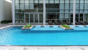 Piscina com água azul cristalina, rodeada por espreguiçadeiras e vasos de plantas.