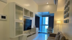 Uma sala de estar moderna com televisão de tela plana, estantes embutidas, um sofá e um espaço de jantar com mesa e cadeiras.