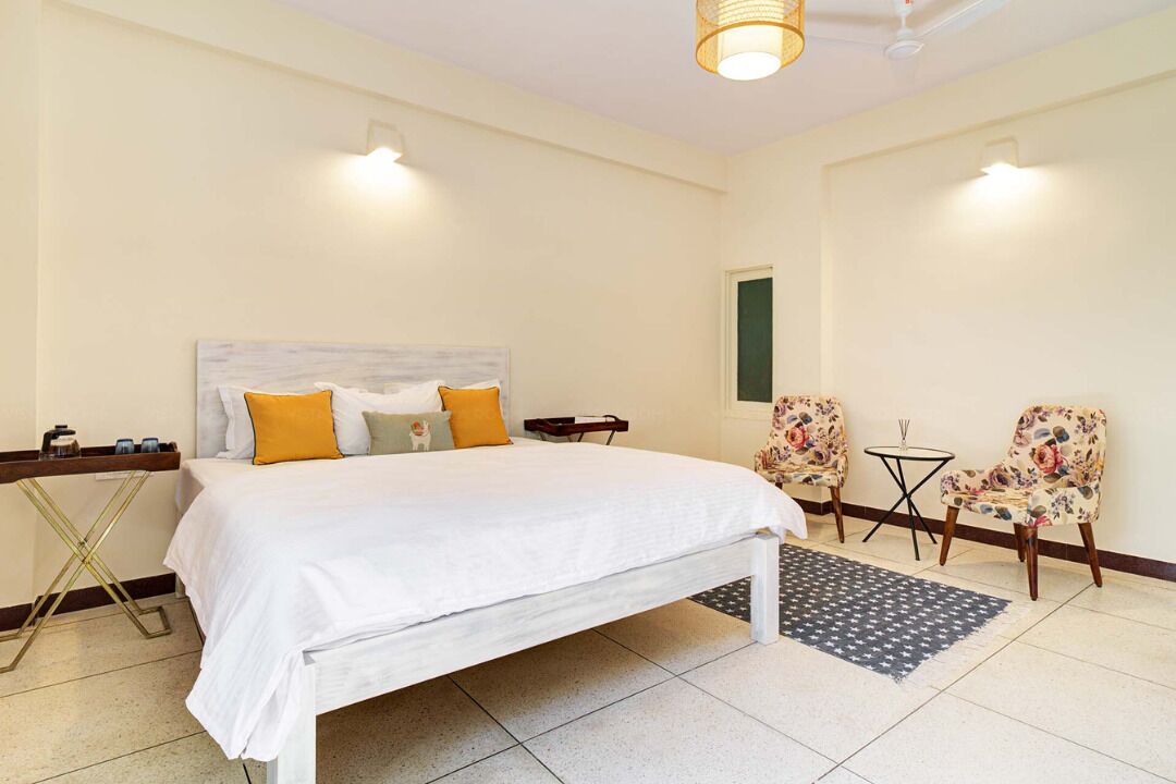 Quarto de hotel com cama, uma mesa pequena, duas cadeiras e um ventilador de teto.