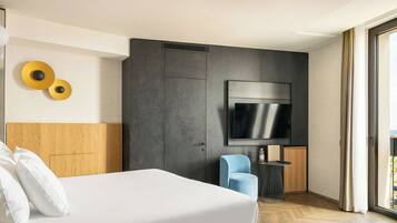 Quarto de hotel moderno com uma cama grande, uma televisão de tela plana na parede, uma mesinha redonda e uma cadeira.