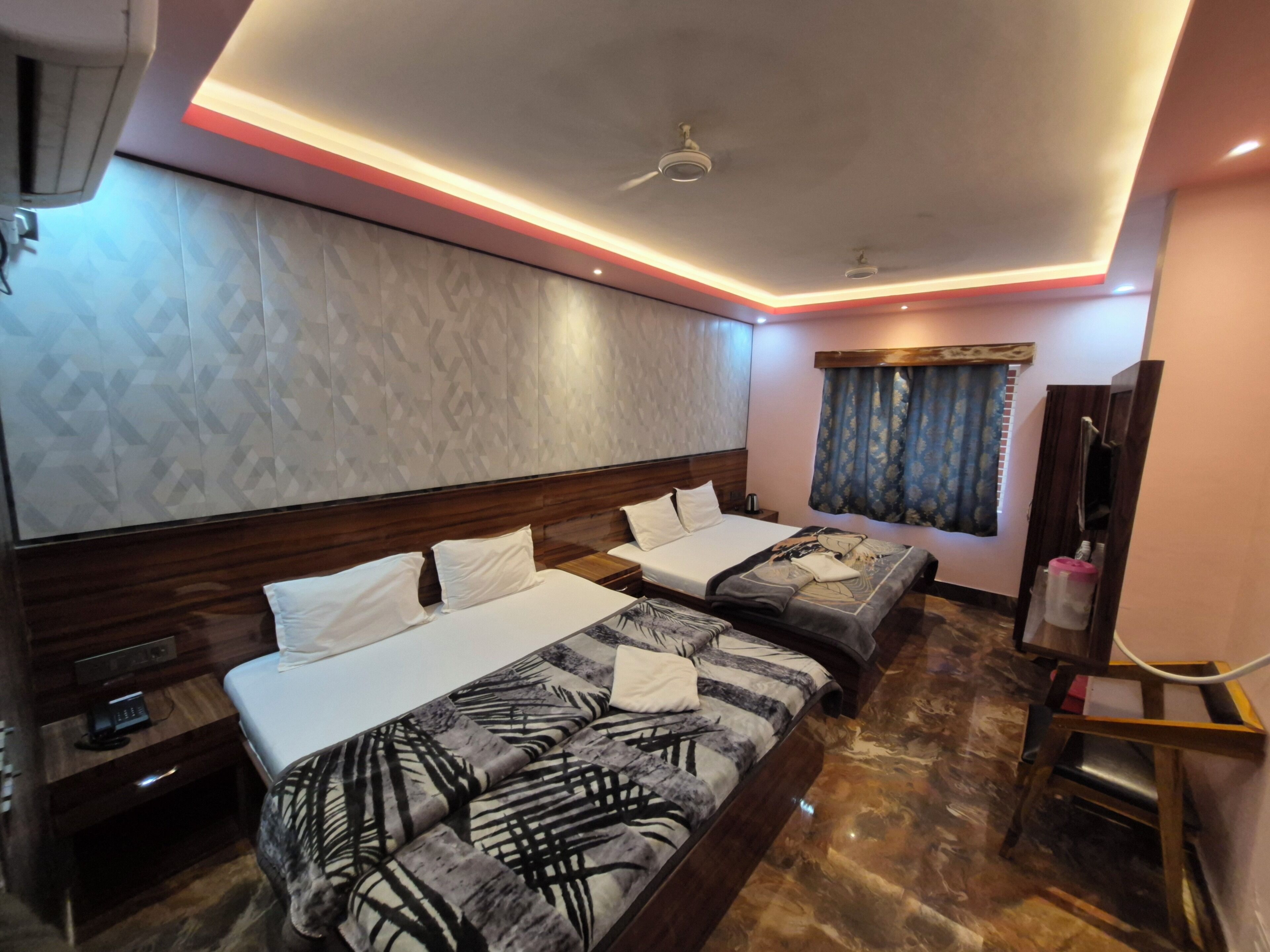 Quarto de hotel com duas camas, ventilador de teto, televisão e minibar.