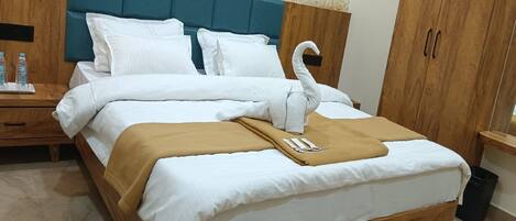 Cama bem arrumada com lençóis brancos e manta marrom, cabeceira de madeira e guarda-roupa de madeira.