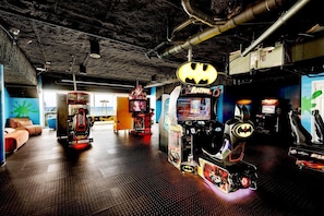 Espaço de jogos com máquinas de arcade, um sofá e vista para o exterior.