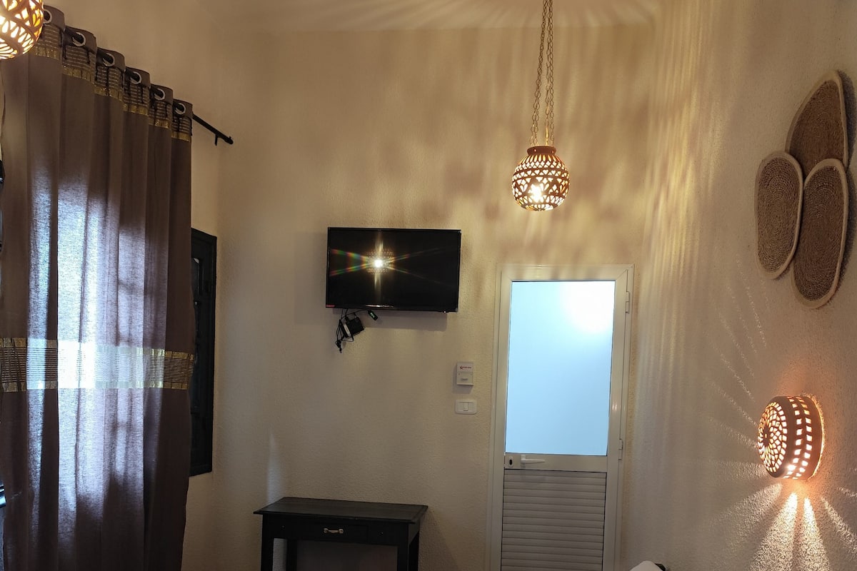 Quarto de hotel com cama, televisão na parede, ventoinha no teto e janela com cortinas.