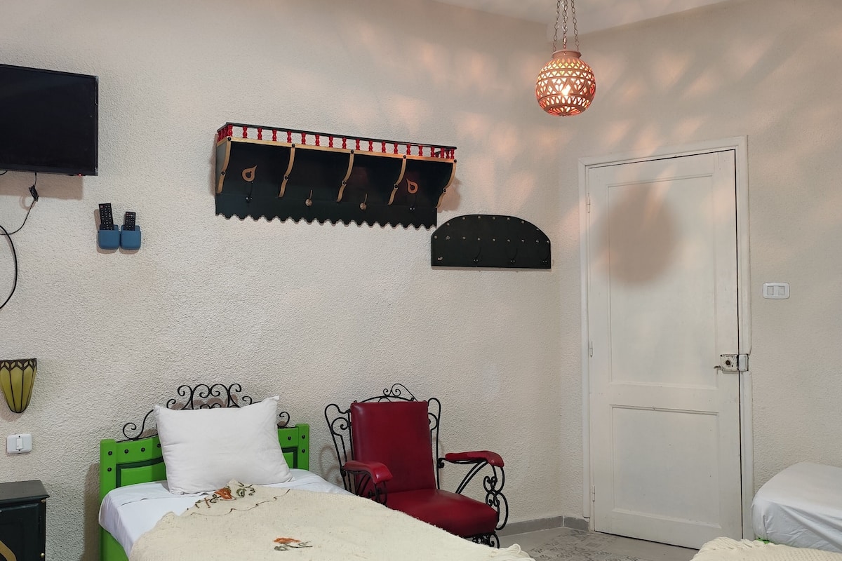 Um quarto com uma cama, uma cadeira, uma televisão e uma porta.