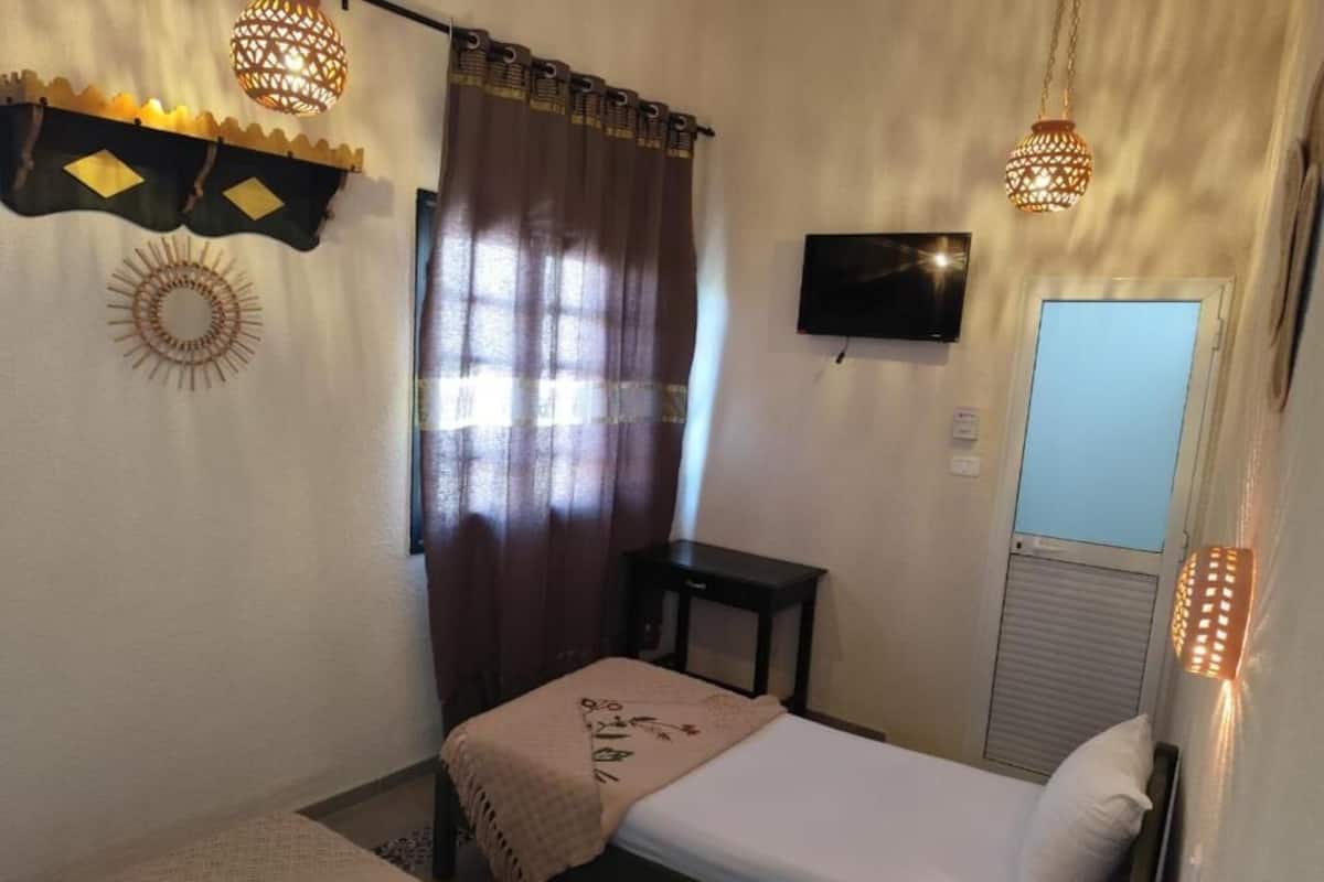 Um quarto pequeno e acolhedor com cama, televisão, mesa de cabeceira e janela com cortinas.