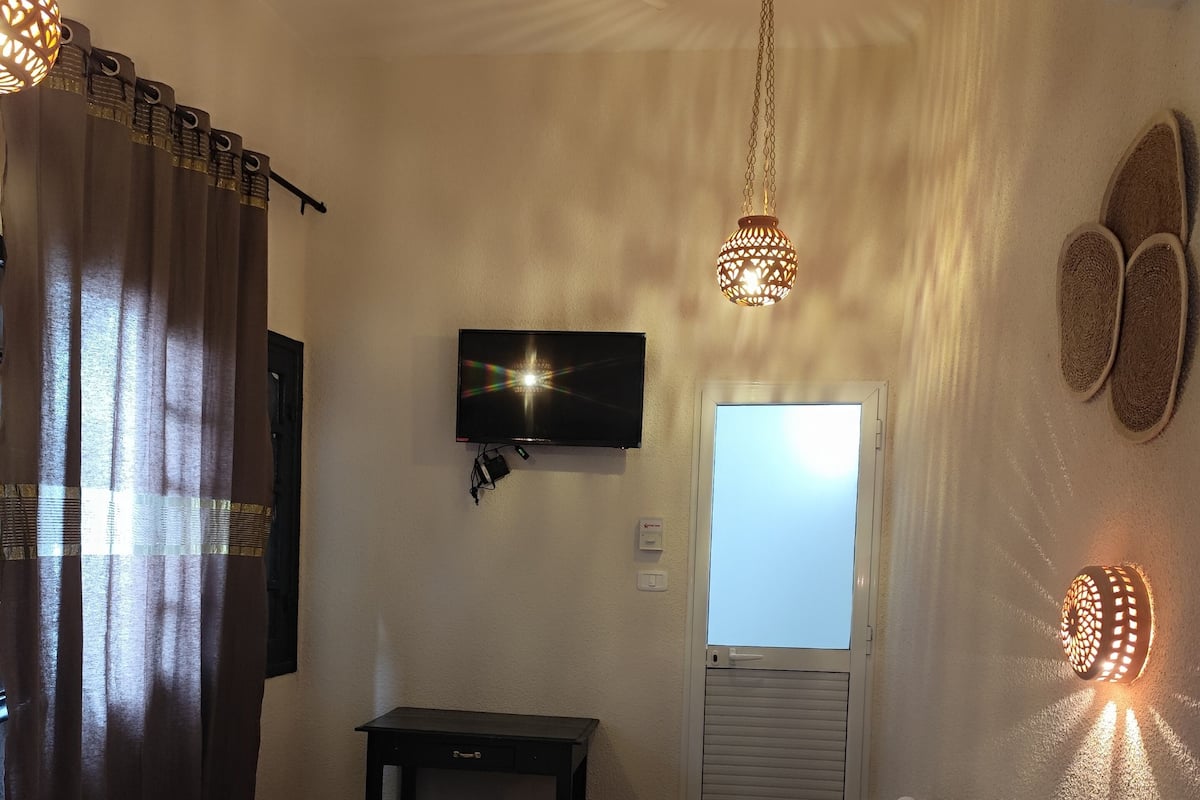 Quarto de hotel com cama, televisão na parede, ventoinha no teto e janela com cortinas.