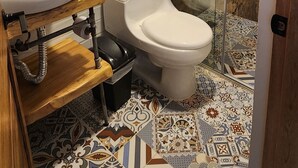 Uma casa de banho com lavatório de madeira, uma sanita branca e uma cabine de duche com porta de vidro.