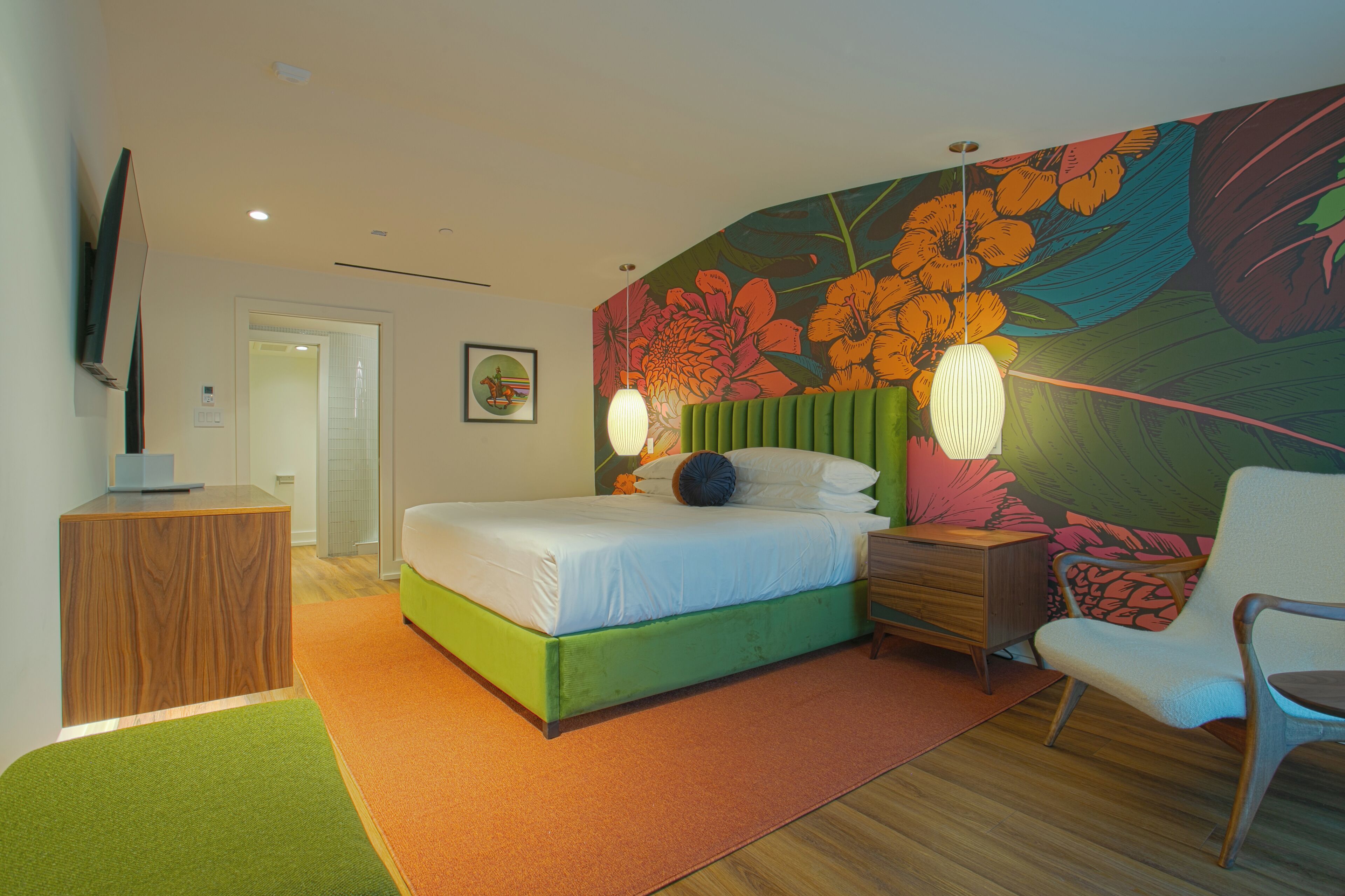 Quarto com cama verde, mesa de cabeceira de madeira, uma cadeira e parede com um mural floral.