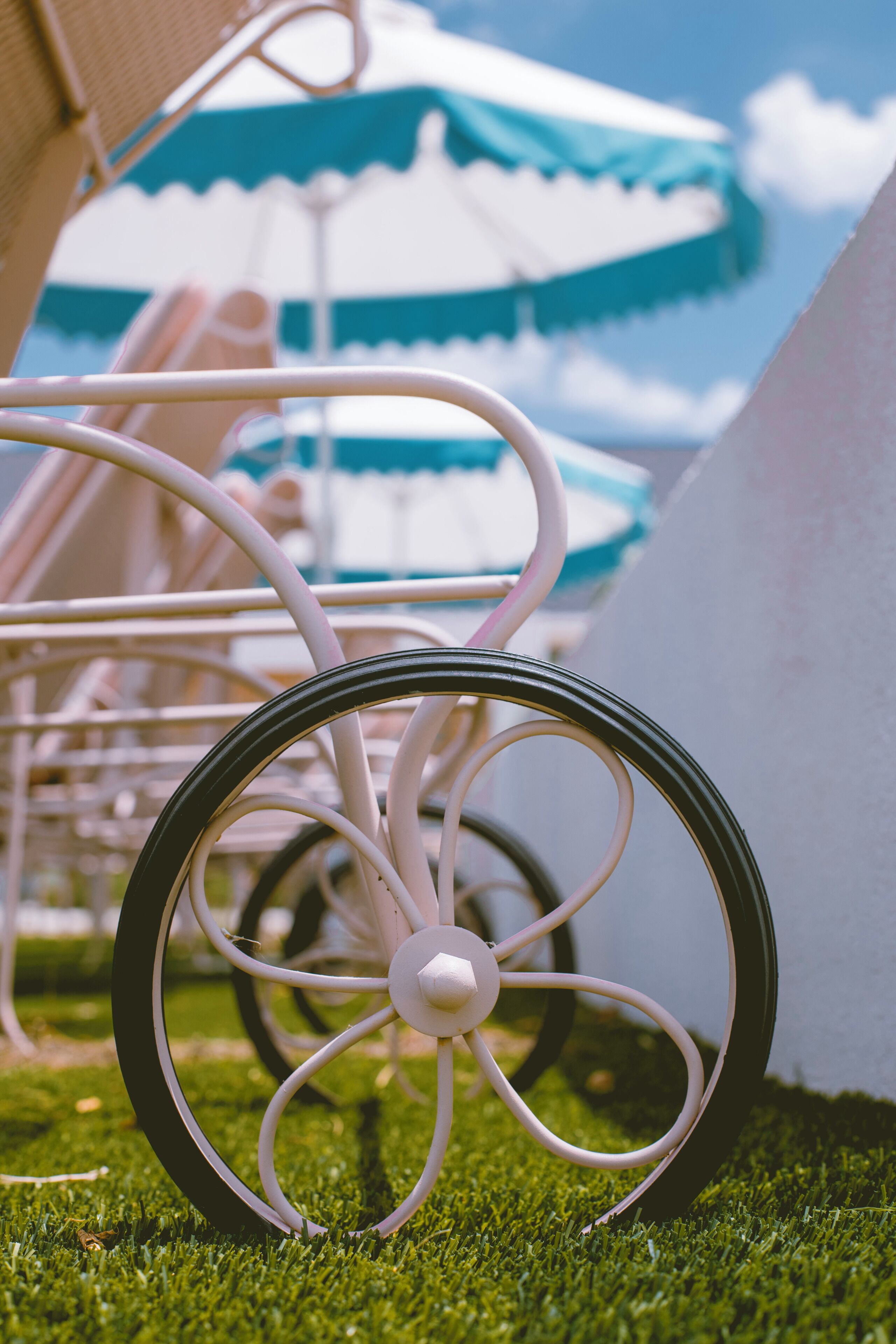 Close-up de uma cadeira de metal branca com uma roda preta, colocada sobre um gramado.