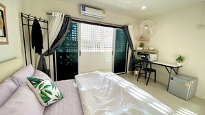 Quarto com cama, escrivaninha, cadeira, um pequeno frigorífico e janela com cortinas.