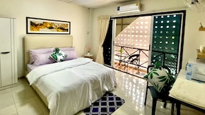 Quarto de hotel com cama, uma pequena mesa com cadeira, janela com cortinas e ar condicionado fixado na parede.