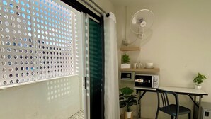 Uma pequena cozinha compacta com micro-ondas, ventilador, mesa e cadeiras.