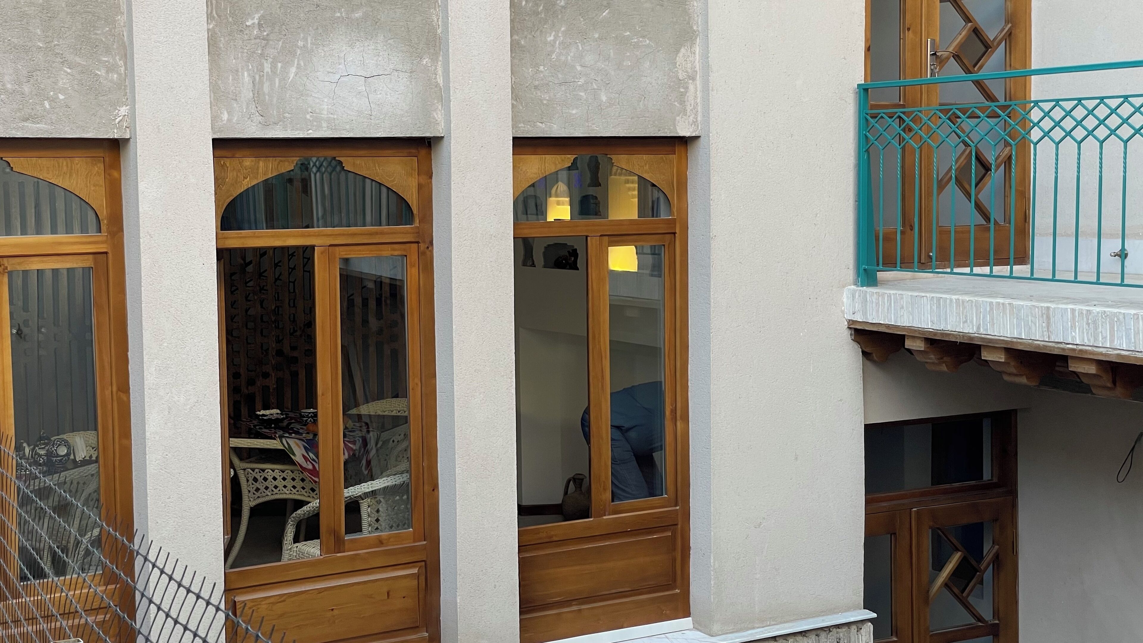 Um edifício com janelas de grandes dimensões emolduradas em madeira, varanda com guarda-corrimão azul-turquesa e parede exterior branca.