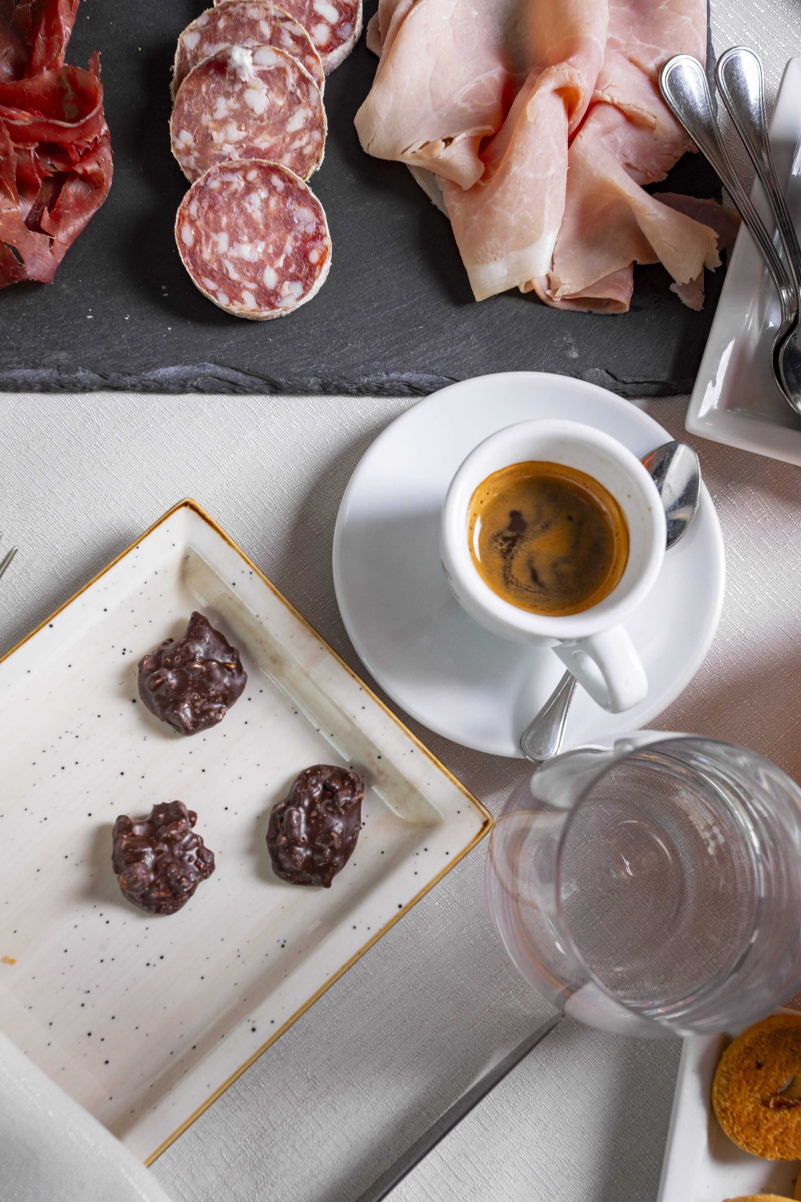 Uma mesa com um prato de salame, uma xícara de café e um jarro de vidro.