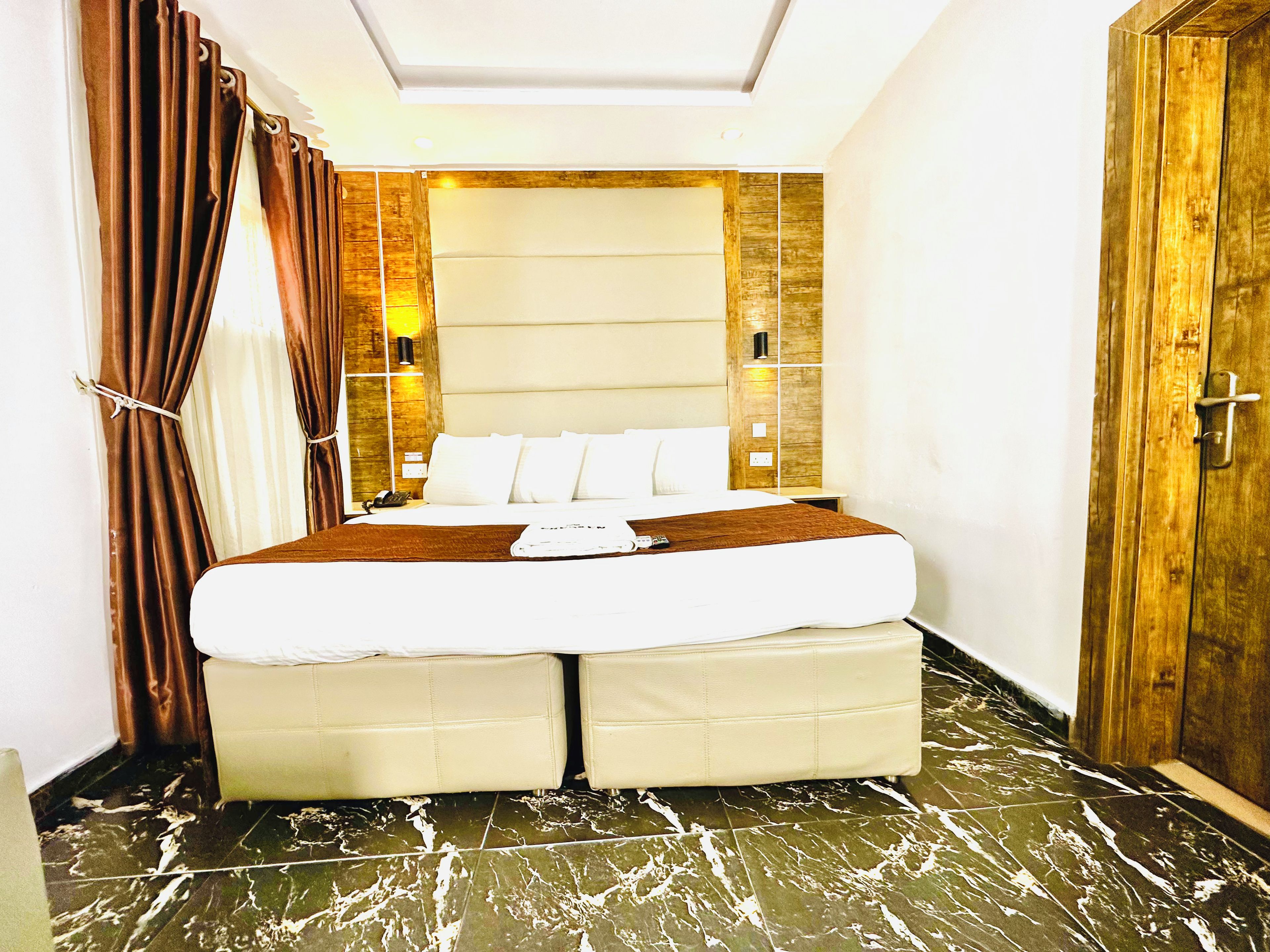 Quarto de hotel com cama, porta de madeira e piso de mármore.