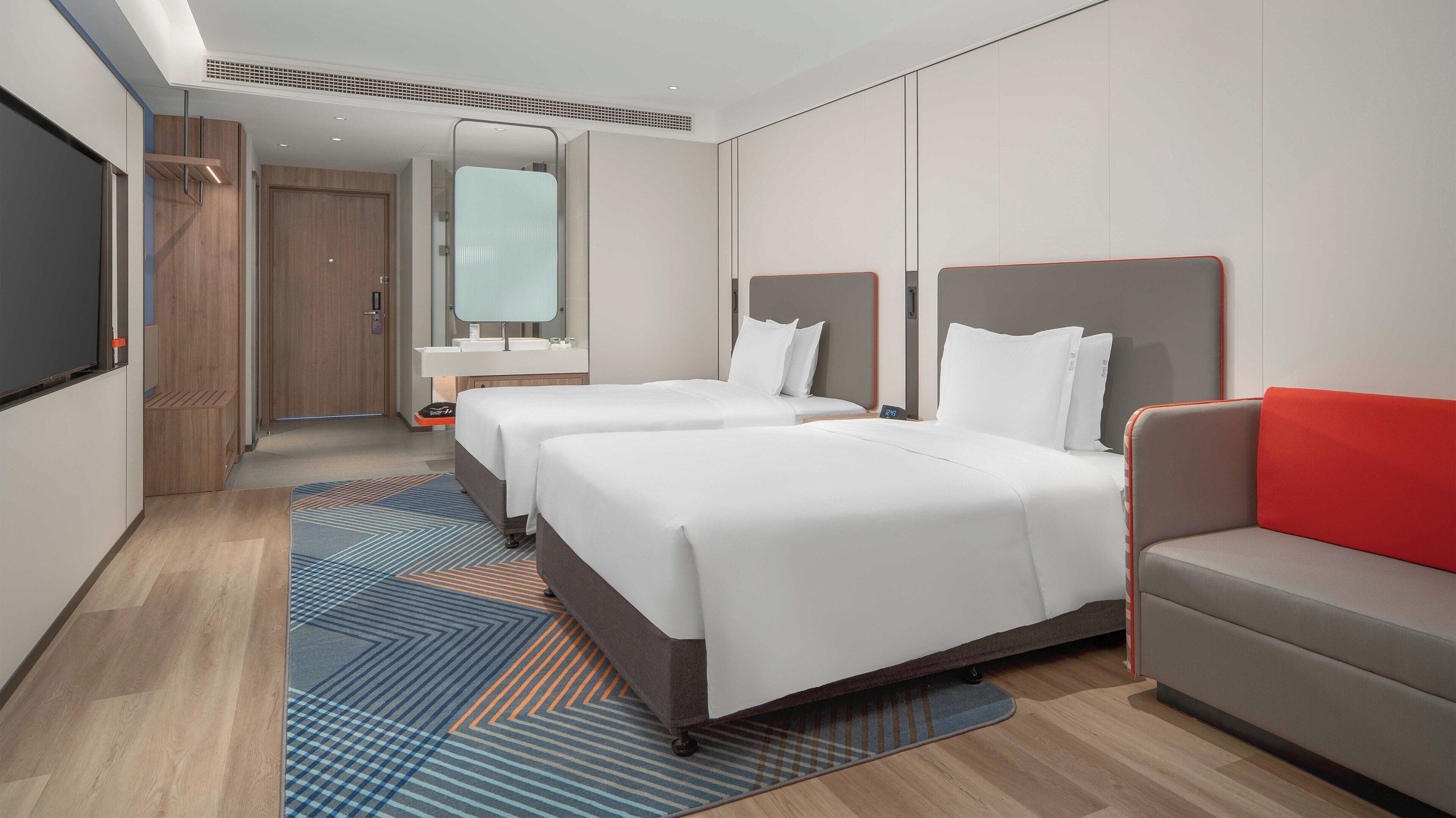 Quarto de hotel com duas camas, um sofá, um banheiro com espelho e uma televisão.