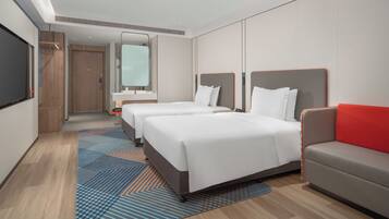 Quarto de hotel com duas camas, um sofá, um banheiro com espelho e uma televisão.