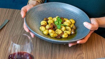 Uma pessoa segurando uma tigela de comida, uma taça de vinho e um prato com comida sobre uma mesa de madeira.