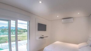 Quarto de hotel moderno com uma janela grande, televisão de tela plana na parede e cama com roupa de cama branca.