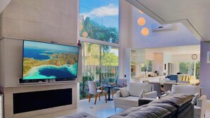 Uma sala de estar moderna com uma televisão grande, assentos confortáveis e vista para o exterior.
