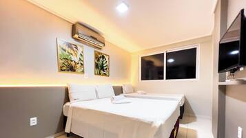 Quarto de hotel com uma cama, uma televisão e duas unidades de ar condicionado fixadas na parede.