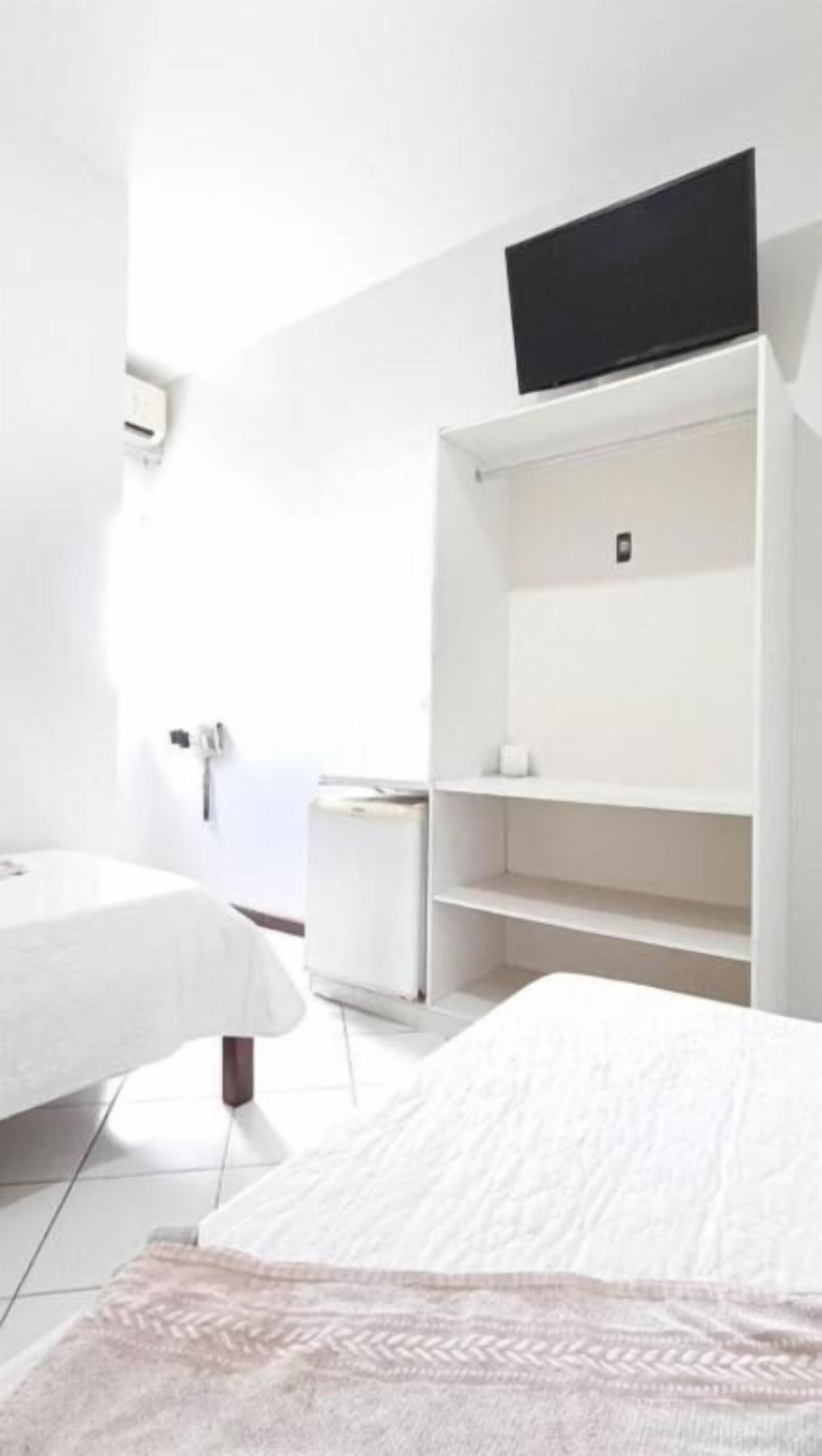 Quarto com cama, televisão na parede e guarda-roupa branco.