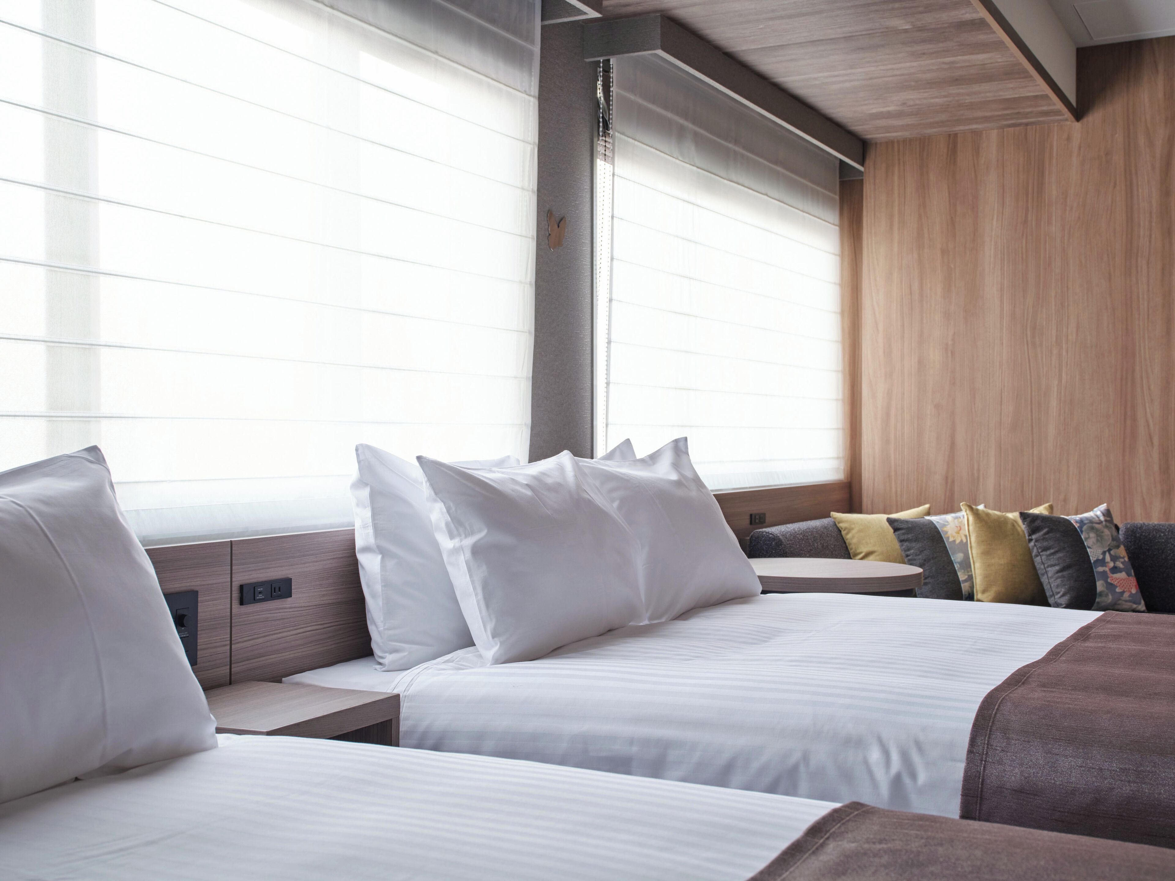 Quarto de hotel moderno com duas camas, uma parede de madeira e uma janela com persianas.