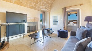 Sala de estar com televisão, uma mesa com objetos decorativos, sofá e vista para o exterior.