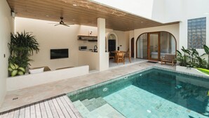 Uma piscina coberta moderna com teto de madeira, área de refeições com mesa e cadeiras, e cozinha com geladeira e armários.
