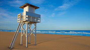 Uma torre salva-vidas numa praia arenosa com o oceano ao fundo.