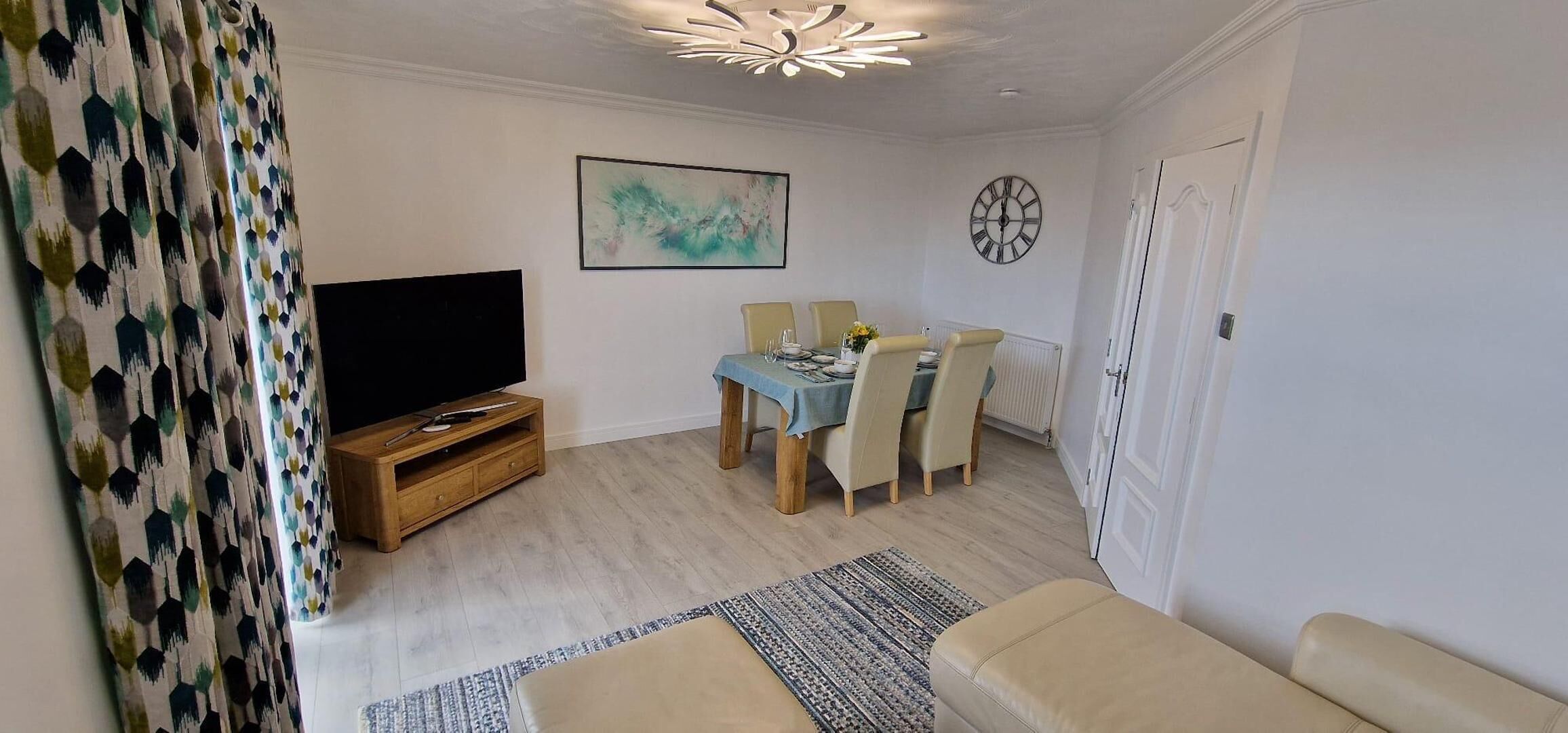 Uma sala de estar com televisão, mesa de jantar, cadeiras e um sofá.