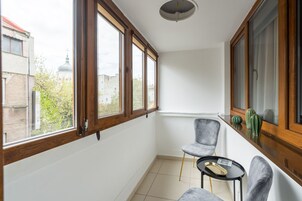 Um quarto pequeno e iluminado, com janelas amplas, parede branca e piso revestido de azulejos.