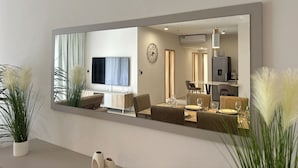 Uma sala de estar moderna com um espelho grande, televisão de tela plana e uma área de jantar com cadeiras e mesa.