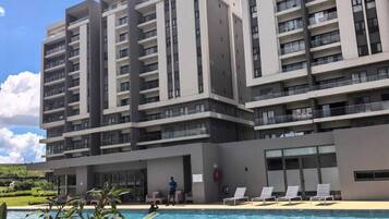 Um hotel moderno com vários andares, piscina e área ajardinada com plantas.