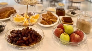 Buffet com diversos alimentos, incluindo frutas, doces e uma bebida sendo servida.