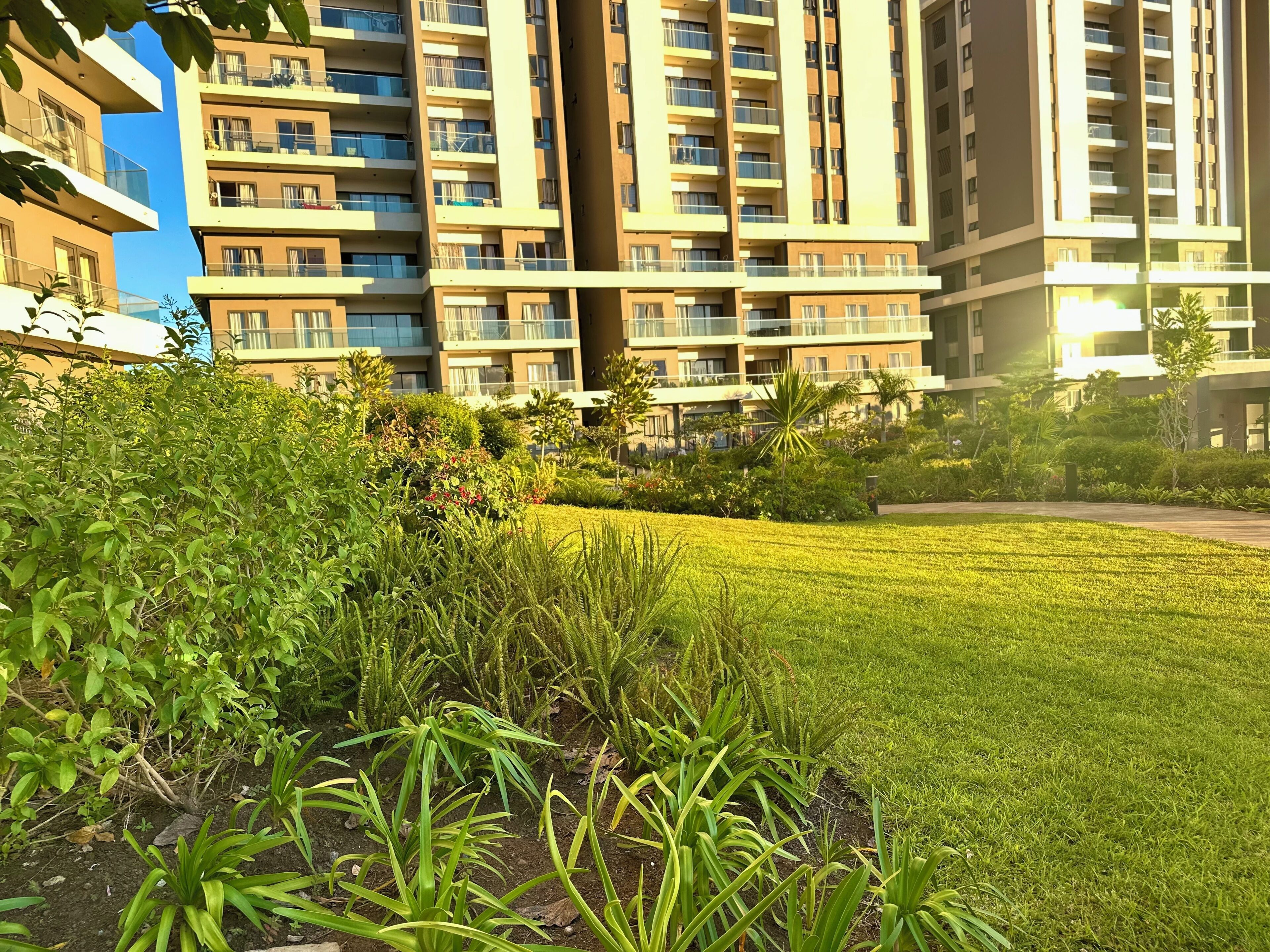 Um edifício residencial moderno com várias varandas, vegetação exuberante e um gramado bem cuidado.
