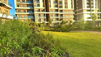 Um edifício residencial moderno com várias varandas, vegetação exuberante e um gramado bem cuidado.