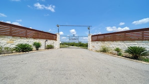 Uma entrada com portão, céu claro, paredes de pedra e uma placa.